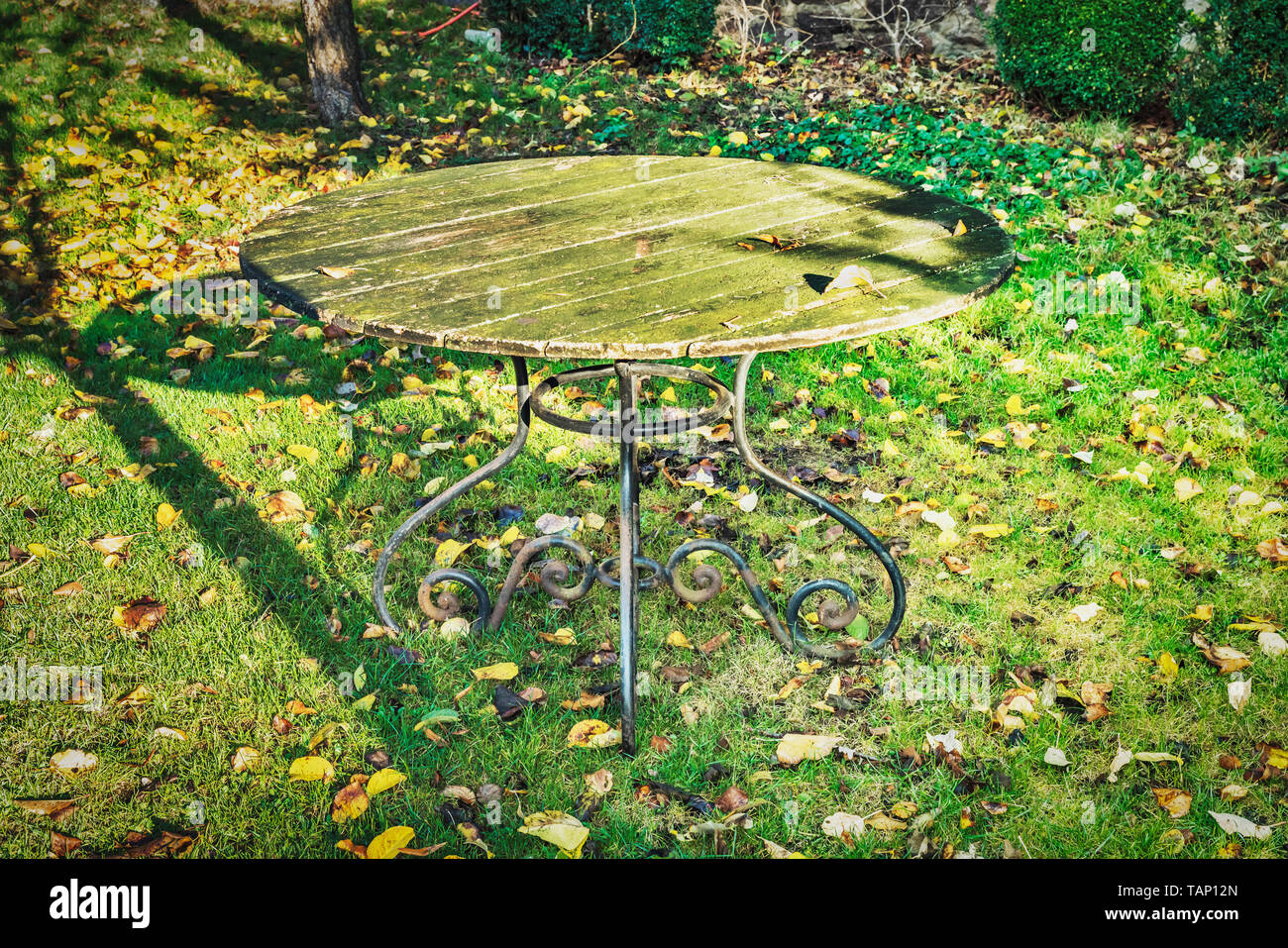 An old round table with metal stand and a wooden tabletop stands in a ...