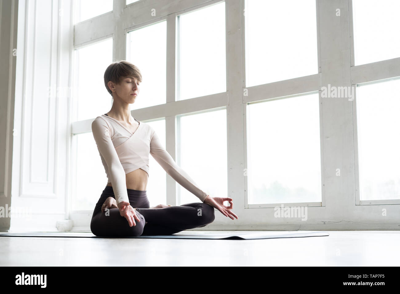 Young attractive smiling woman practicing yoga, sitting in Half Lotus ...