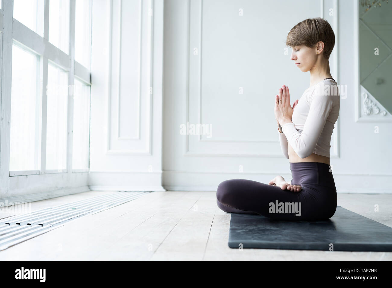 Young attractive smiling woman practicing yoga, sitting in Half Lotus ...