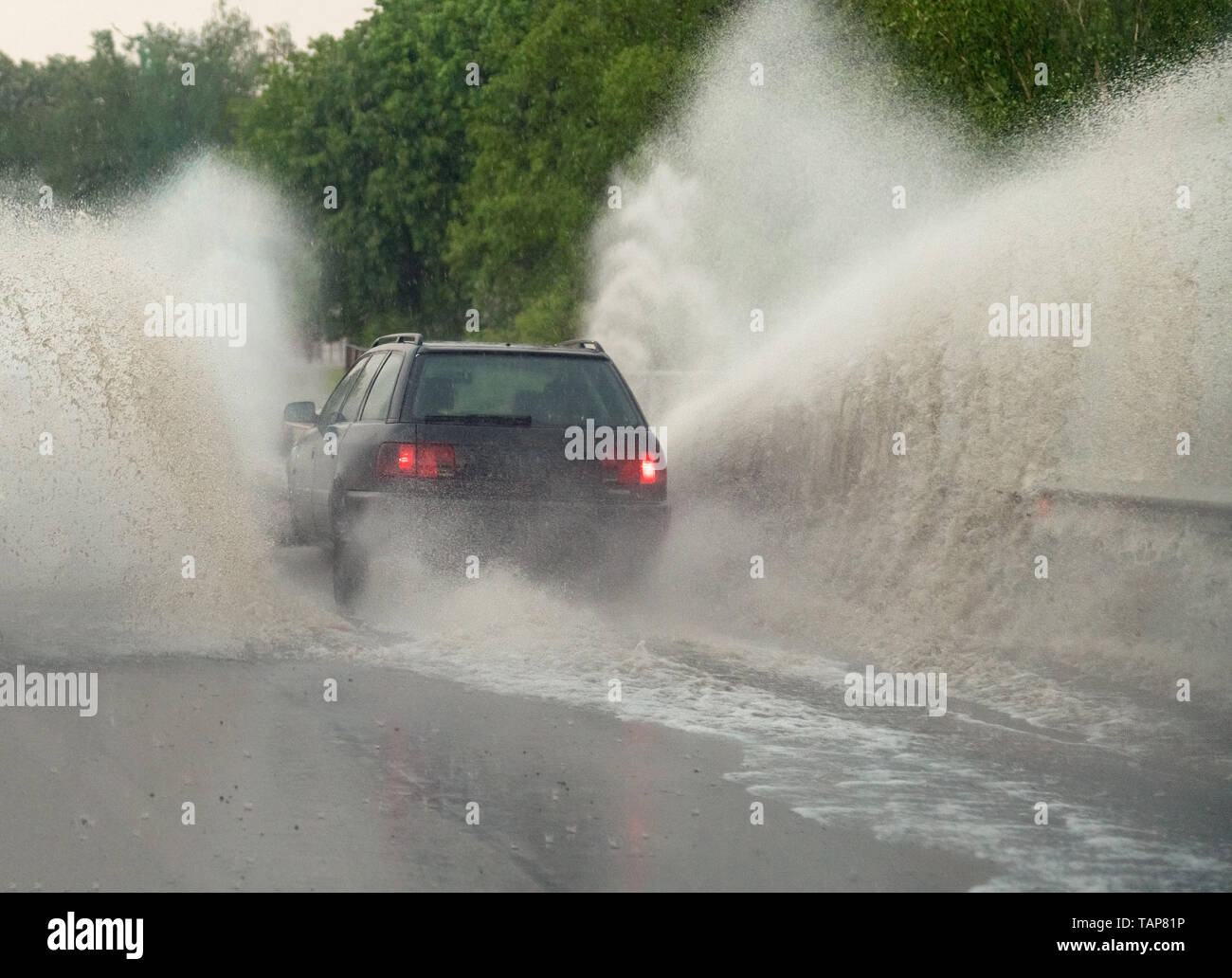 Car runs into big puddle at heavy rain, water splashing over the car ...