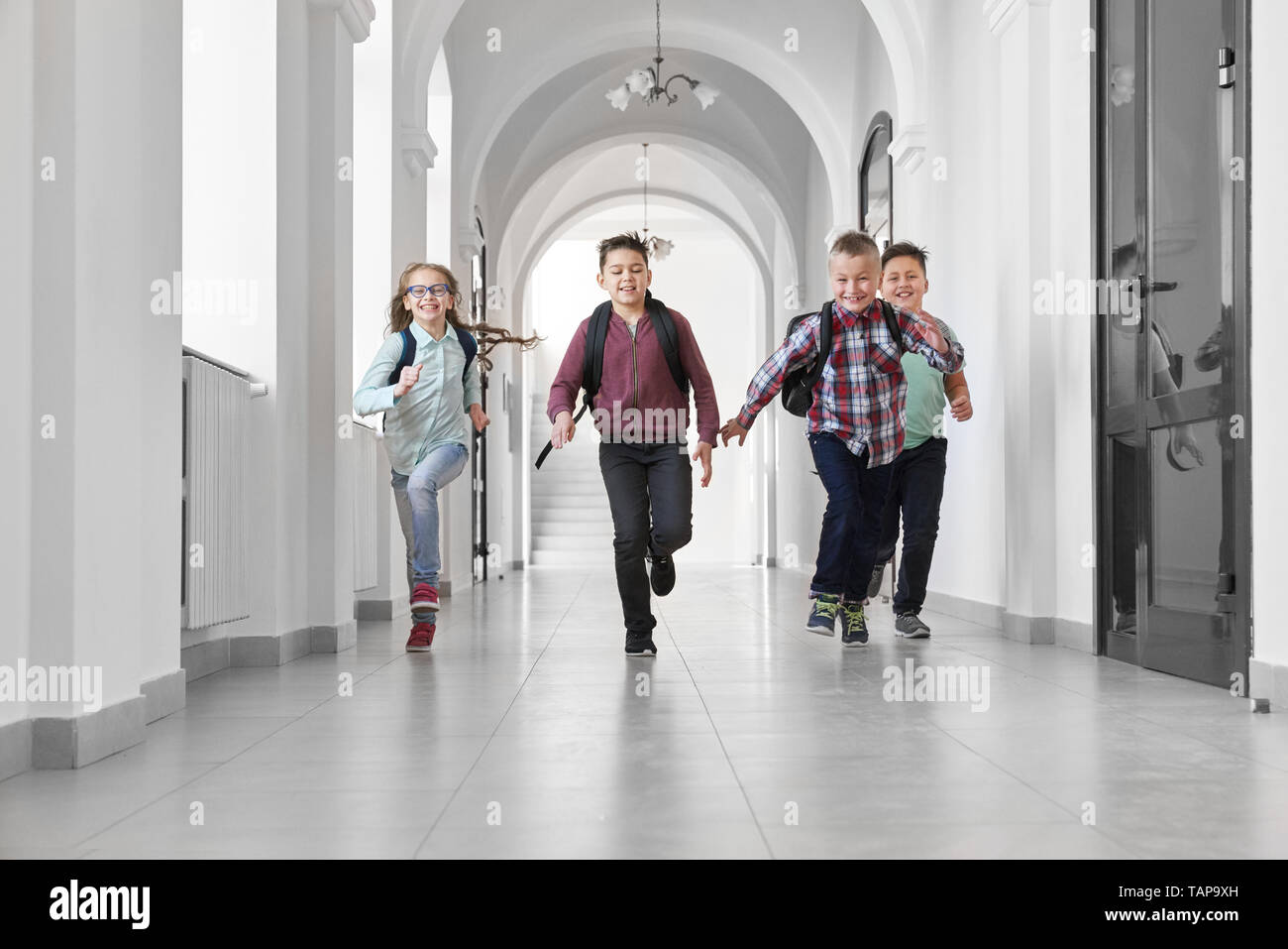 Group of happy, positive schoolchildren running in long hallway of ...