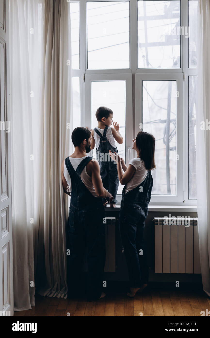 father and mother are holding their son near the window and smile Stock ...