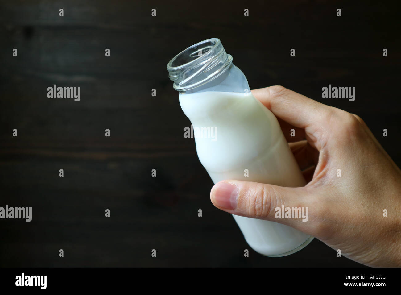Man's hand holding a bottle of milk ready to drink, dark brown wall ...