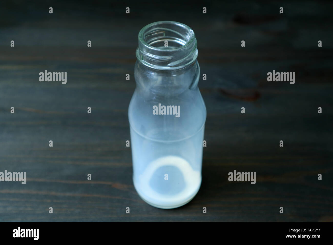 Empty milk glass bottle after drinking isolated on dark colored wooden ...