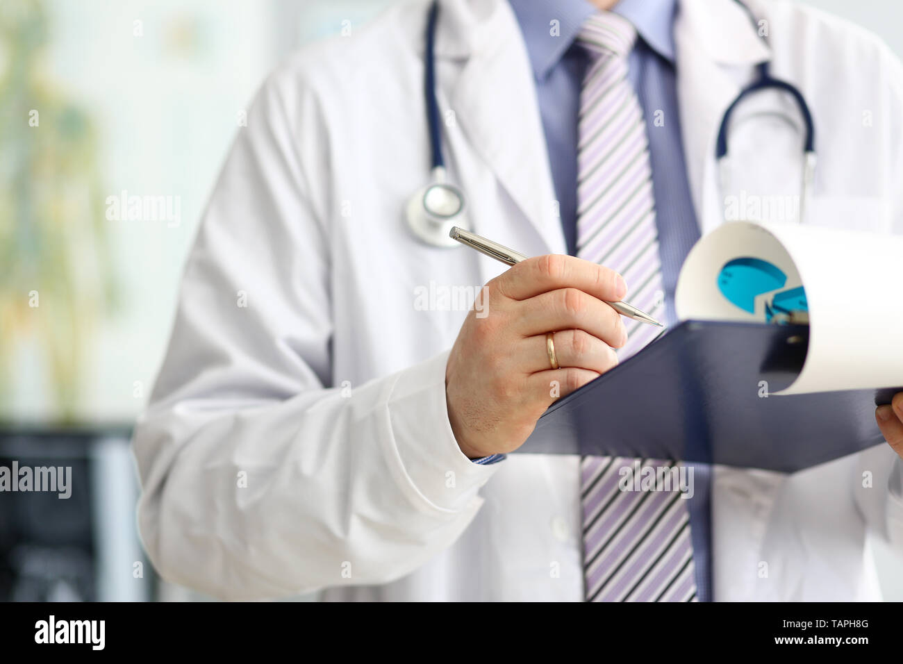Male doctor checking medical procedure results in document clipped to ...