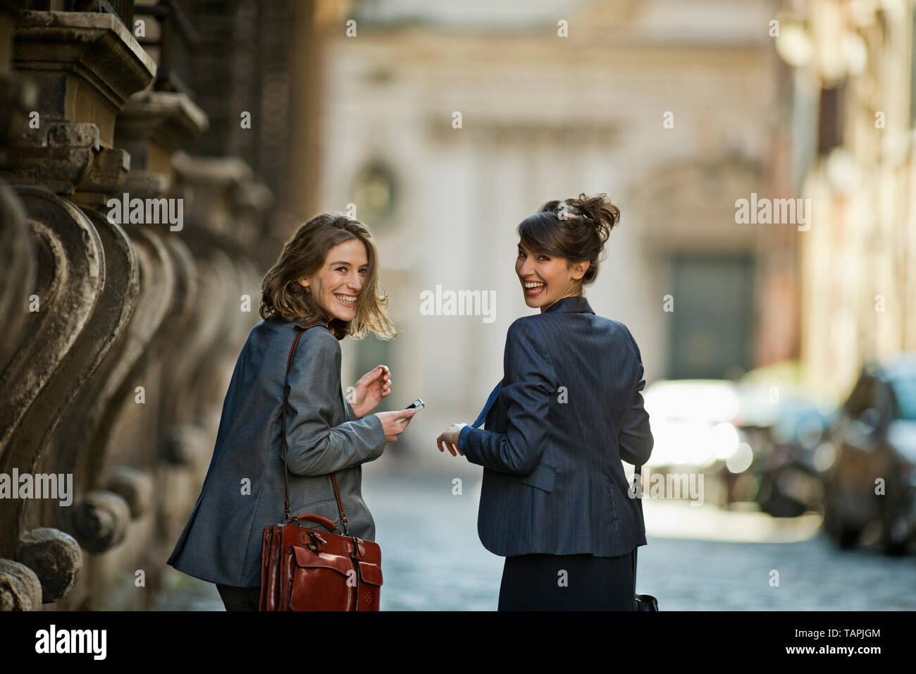Two laughing young office girls look over their shoulder while heading ...