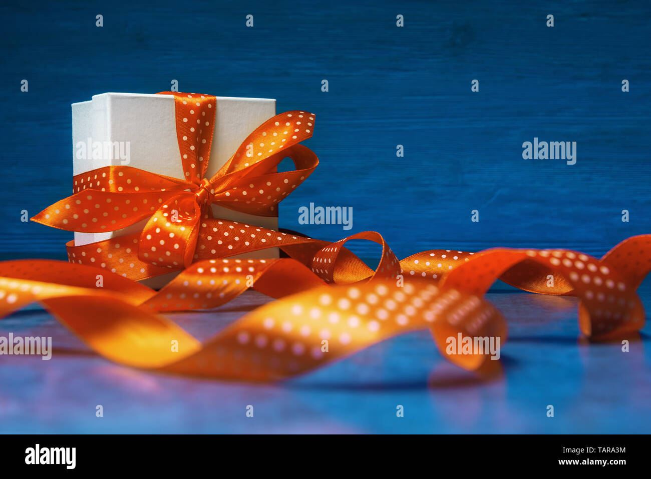Gift box with spotted orange ribbon against blue background Stock Photo ...