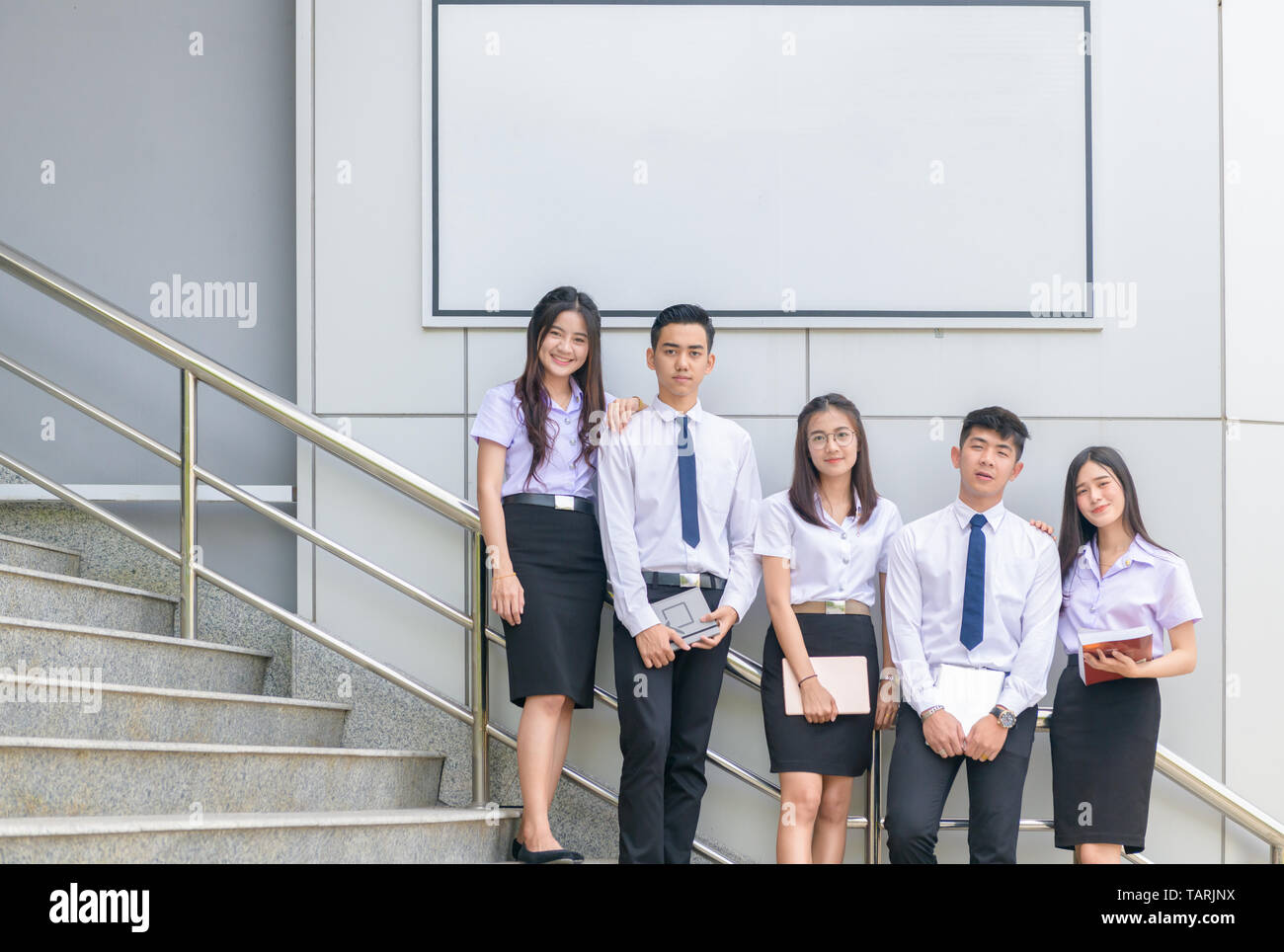 group of young students stand and smile on stairs with white billboard ...