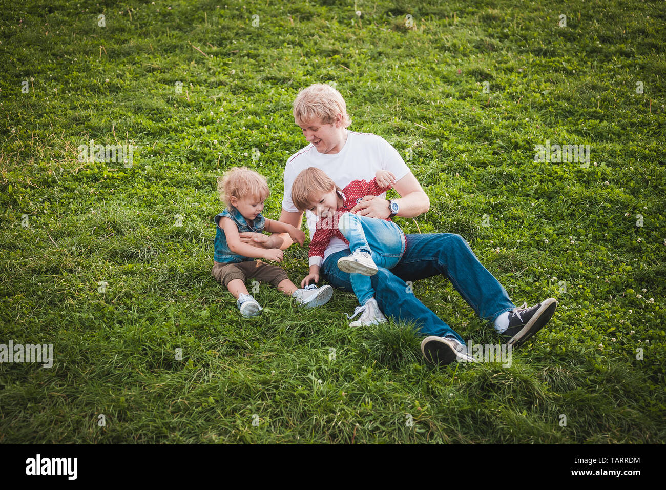 Happy father with two little sons in park in sunny day on green lawn ...