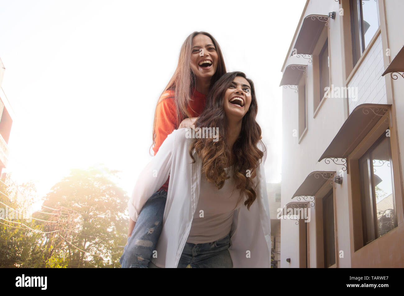 Woman carrying friend on her back walking outdoors in a street Stock ...