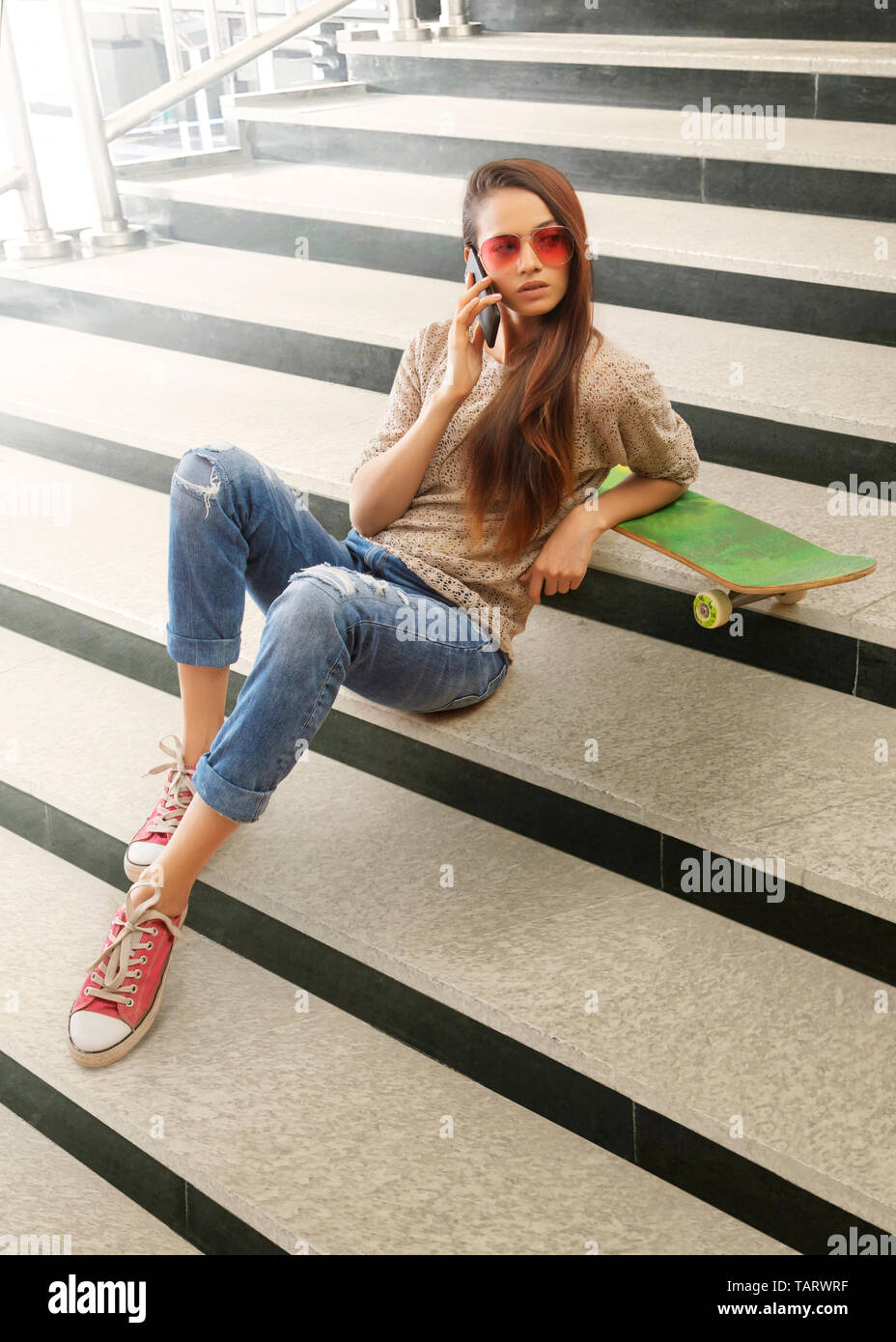 Woman sitting on steps with skateboard talking on mobile phone Stock ...