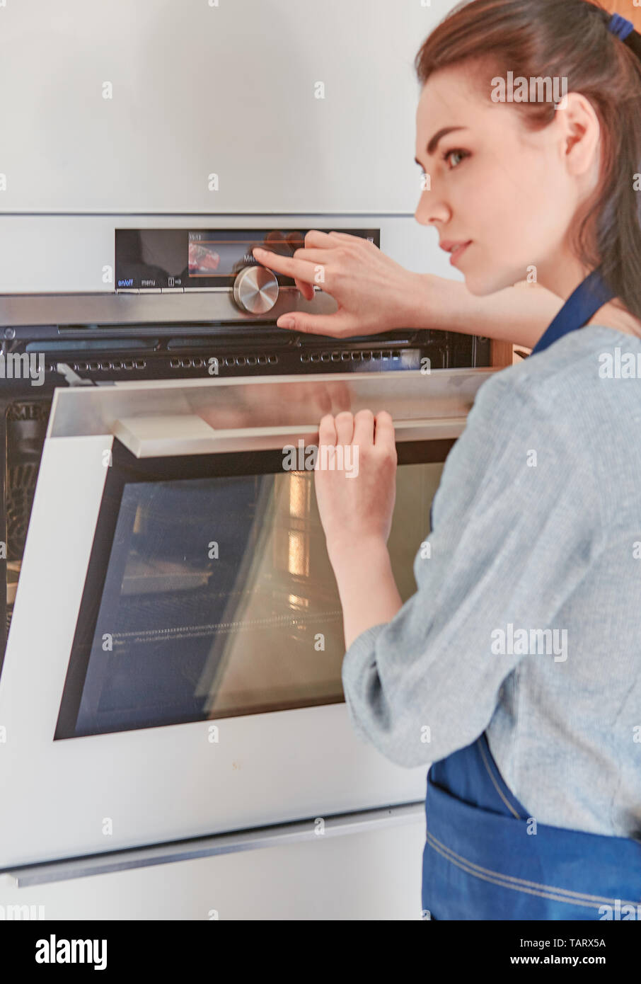 Beautiful woman in the kitchen, waiting with the front of the oven ...