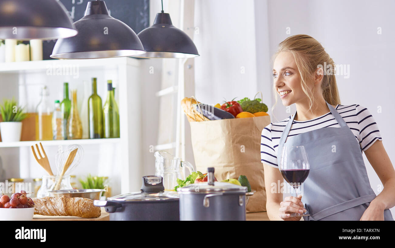 Beautiful woman in kitchen is drinking red wine Stock Photo - Alamy