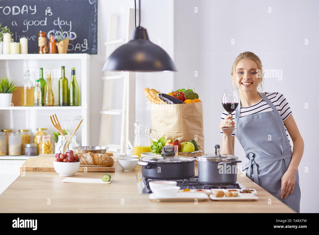 Beautiful woman in kitchen is drinking red wine Stock Photo - Alamy