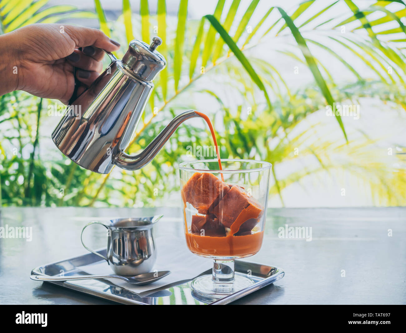 Hand pouring Thai milk tea from stainless steel jug on Thai tea ice ...
