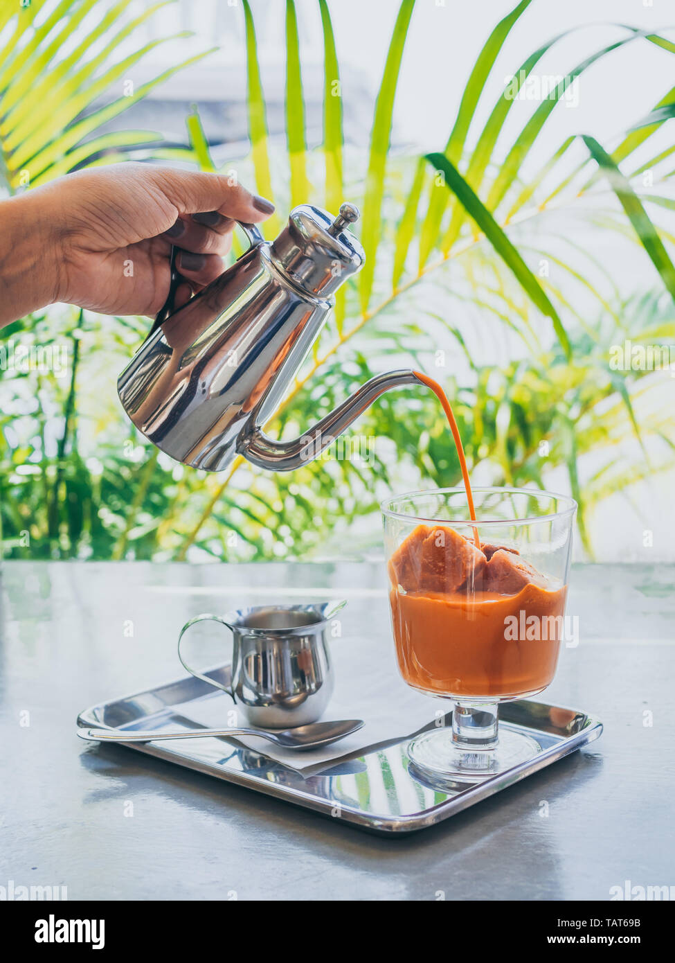 Hand pouring Thai milk tea from stainless steel jug on Thai tea ice ...