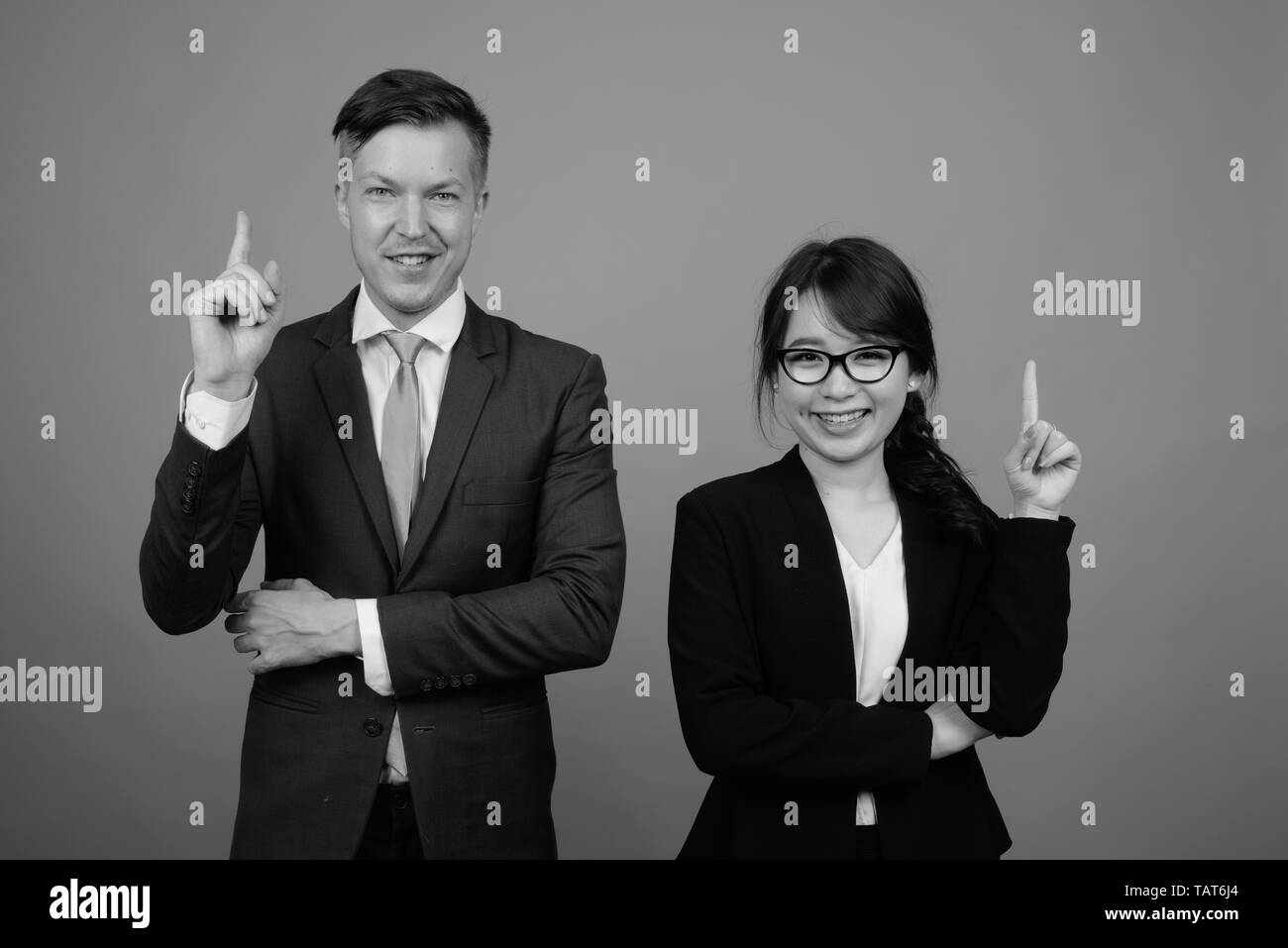 Young businessman and young Asian businesswoman against gray bac Stock ...