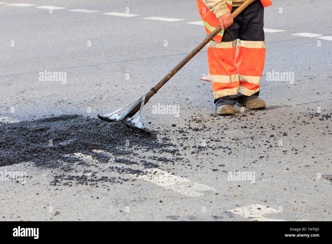 A road worker levels a fresh asphalt by a wooden level on a repaired ...