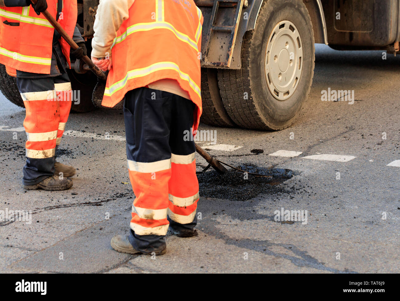 Two road builders with a shovel and a rover line up fresh asphalt on ...