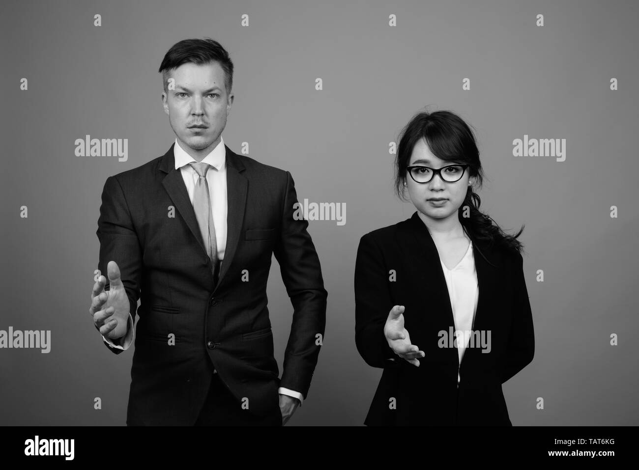 Young businessman and young Asian businesswoman against gray bac Stock ...