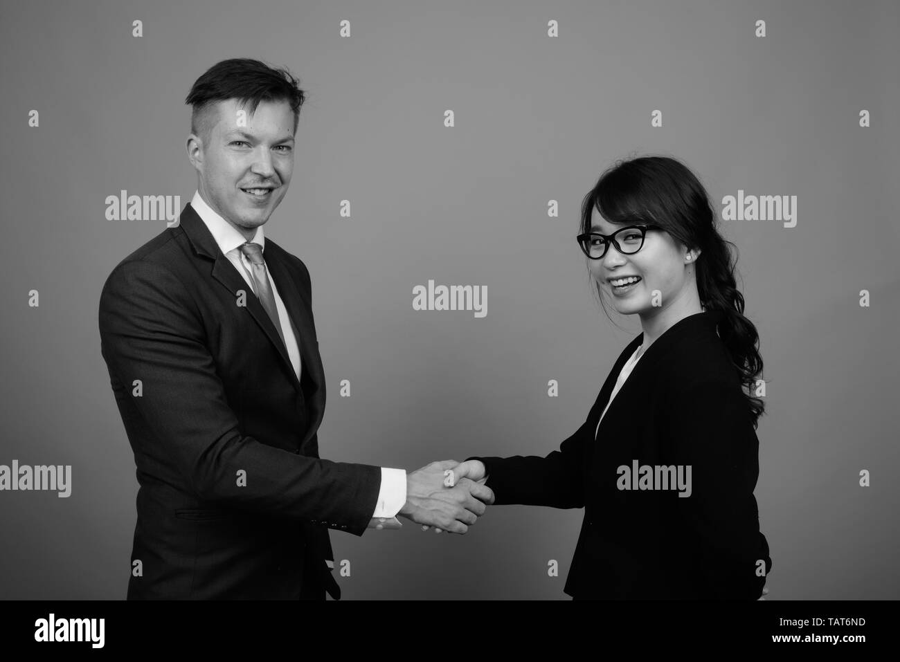 Young businessman and young Asian businesswoman against gray bac Stock ...