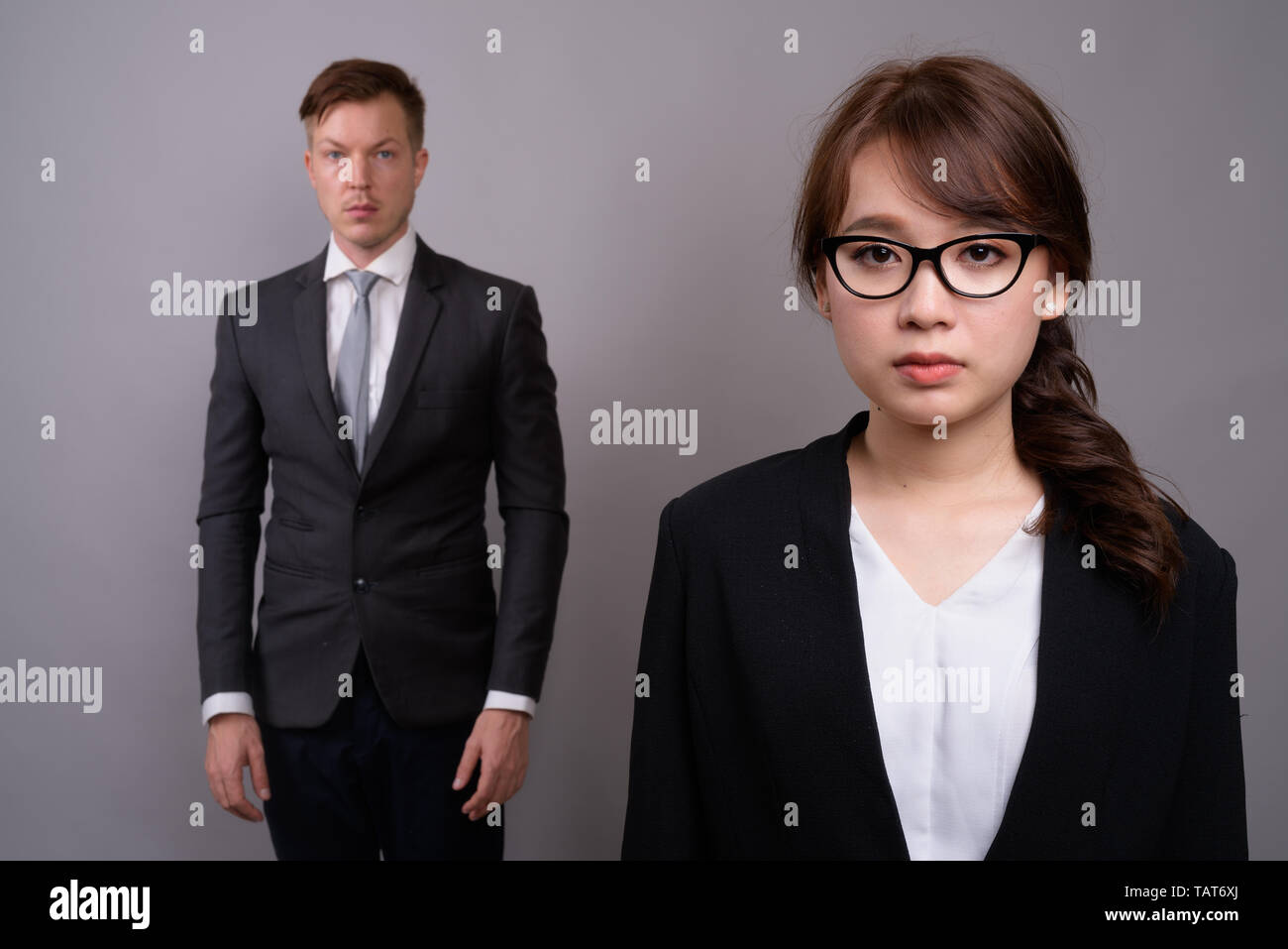 Young businessman and young Asian businesswoman against gray bac Stock ...