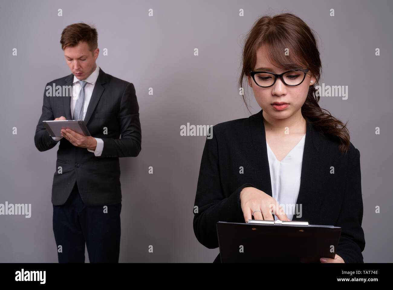 Young businessman and young Asian businesswoman against gray bac Stock ...
