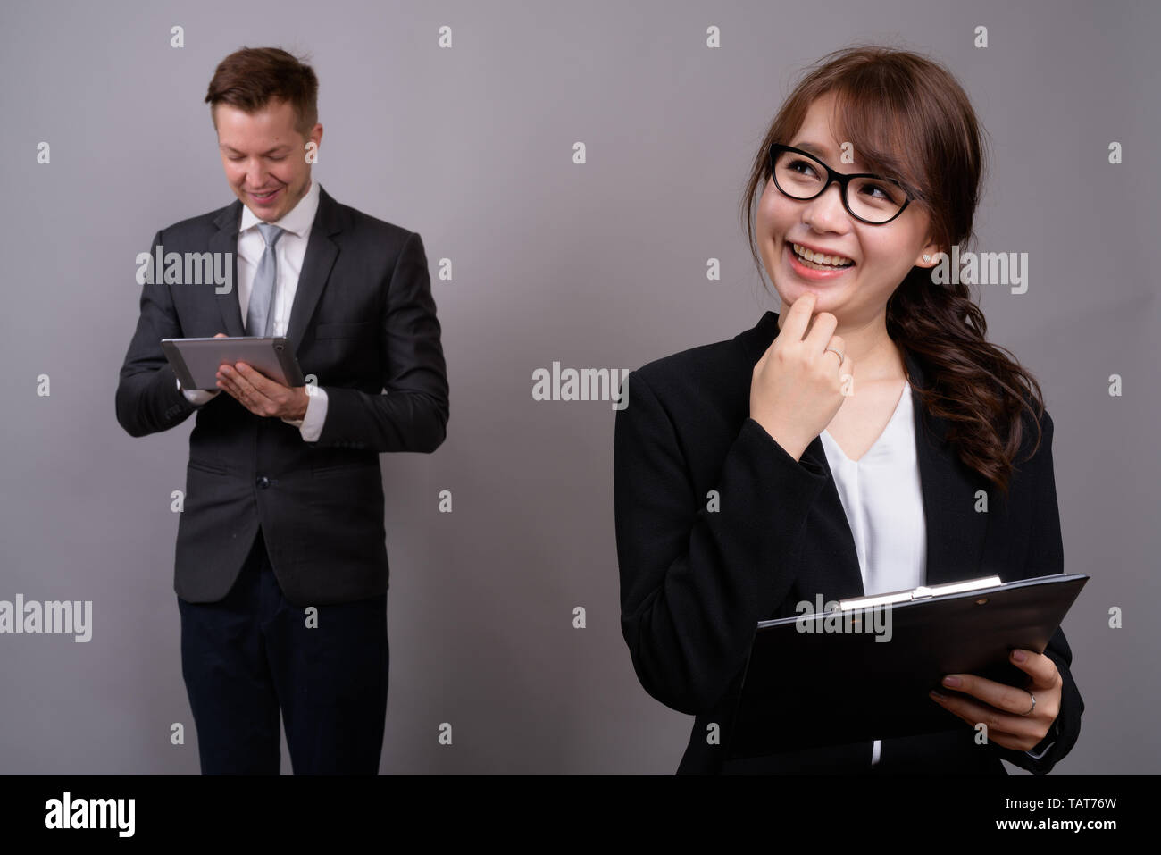 Young businessman and young Asian businesswoman against gray bac Stock ...