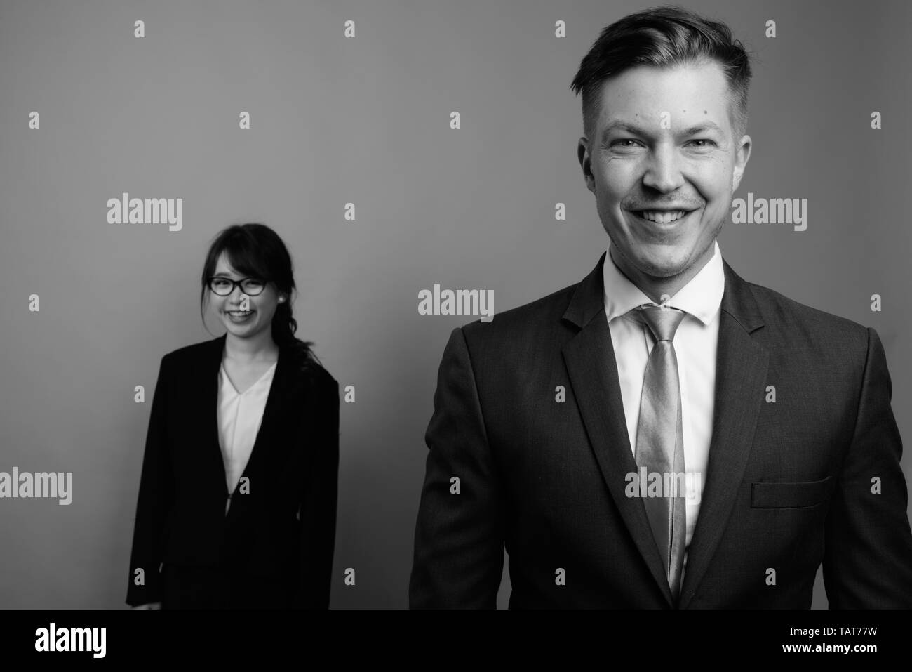 Young businessman and young Asian businesswoman against gray bac Stock ...