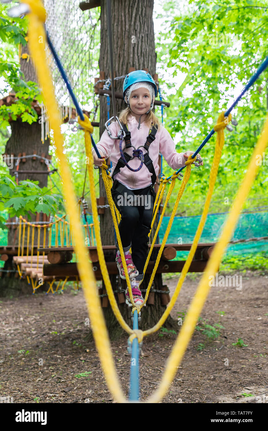 Little girl in harness crossing rope bridge in forest in a ropes course ...