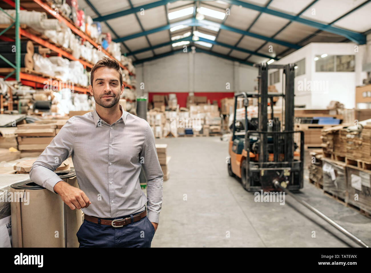 Portrait of a smiling warehouse manager leaning against some stock with ...