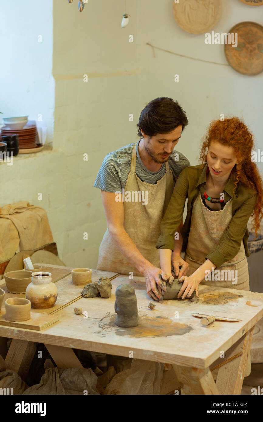 Processing wet clay. Bearded focused teacher explaining his student ...
