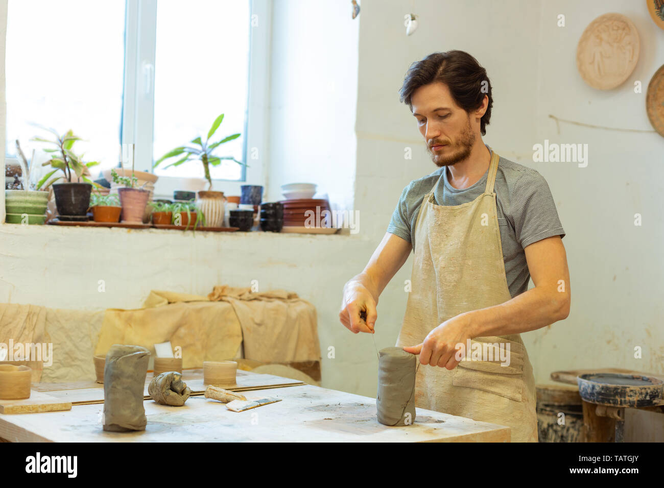 Bright studio. Concentrated bearded guy being a professional pottery ...
