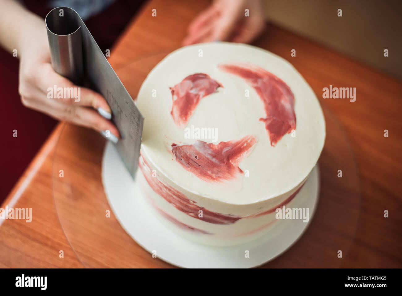 Confectioner using a knife to smooth the sides and top of the cake ...