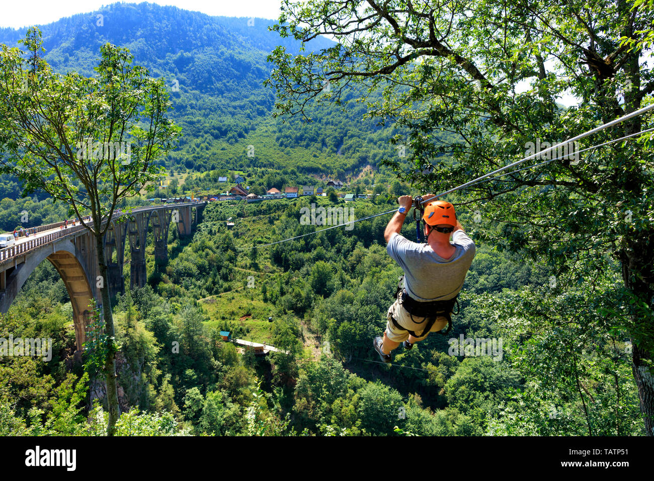 A man crosses over a long cable car over a mountain and forest across ...
