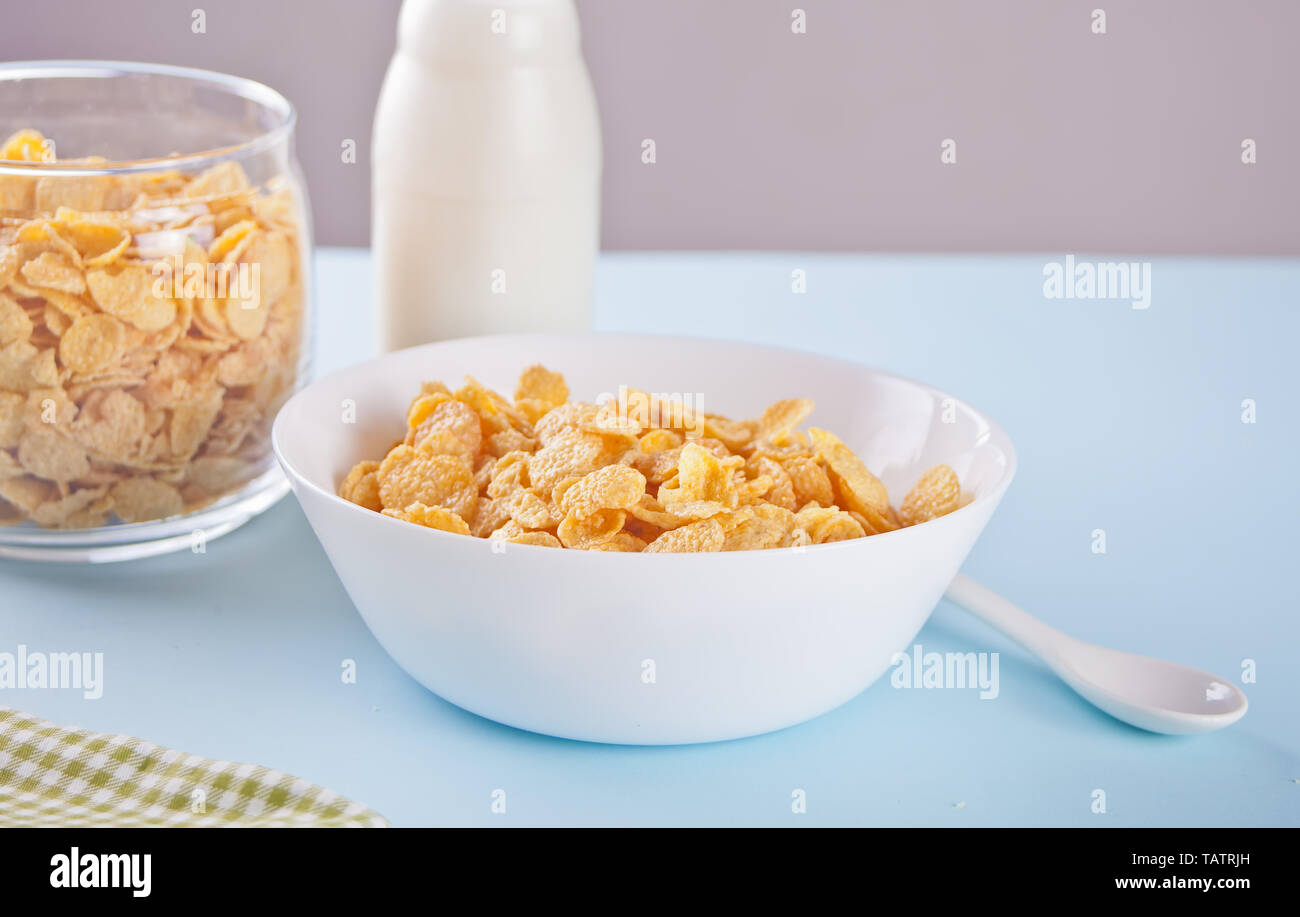 A bowl of dry corn flakes cereal and bottle if milk on the blue table ...