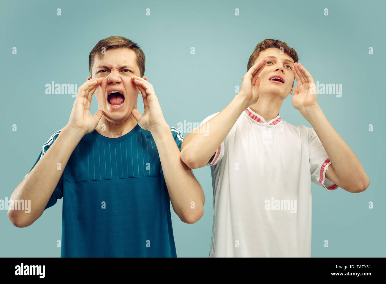 Two young men standing in sportwear isolated on blue studio background ...