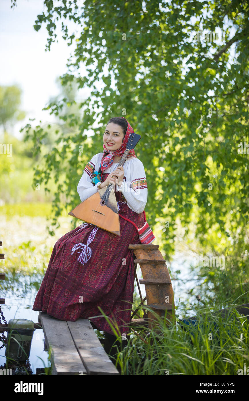 Young smiling woman in traditional russian clothes sits on the small ...