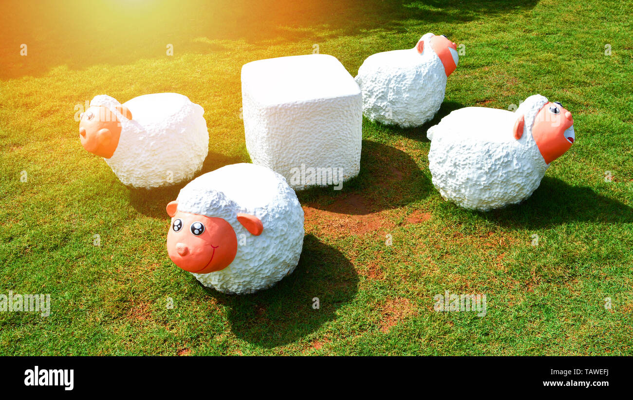 Group of cute white sheep statue on grass in the garden park for bench ...