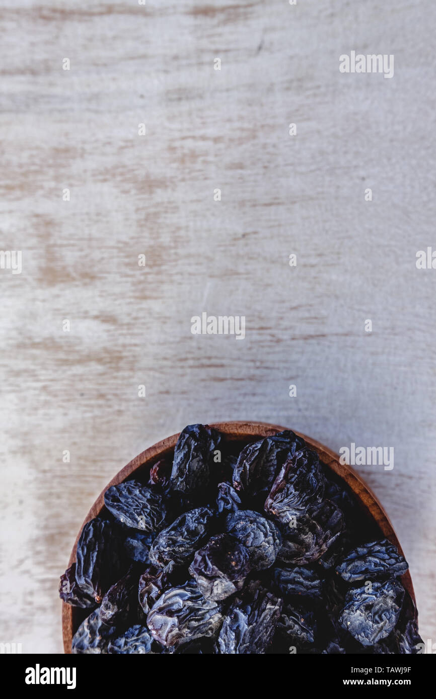 Dark blue raisins in a wooden bowl on a bright white background. Close ...