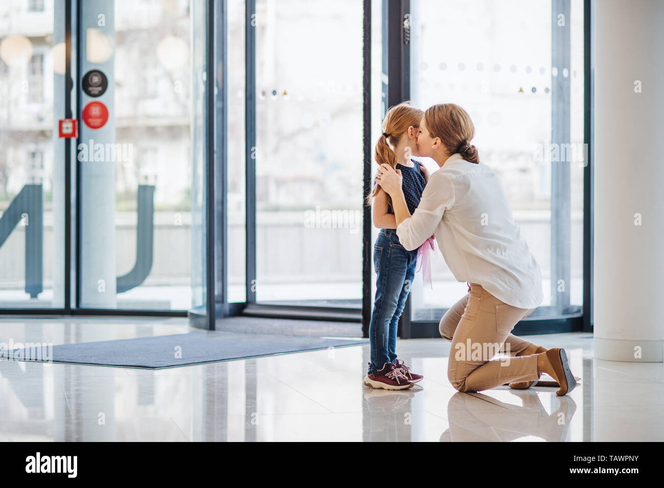 A mother saying goodbye to small daughter in office building, nursery ...