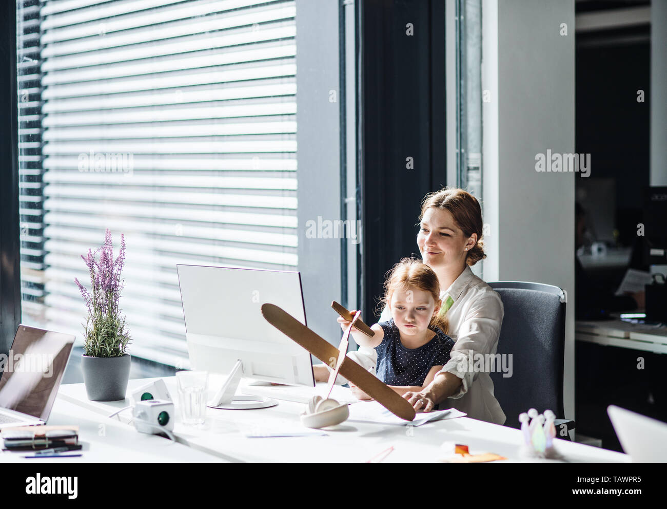 A businesswoman with small daughter sitting in an office, working and ...