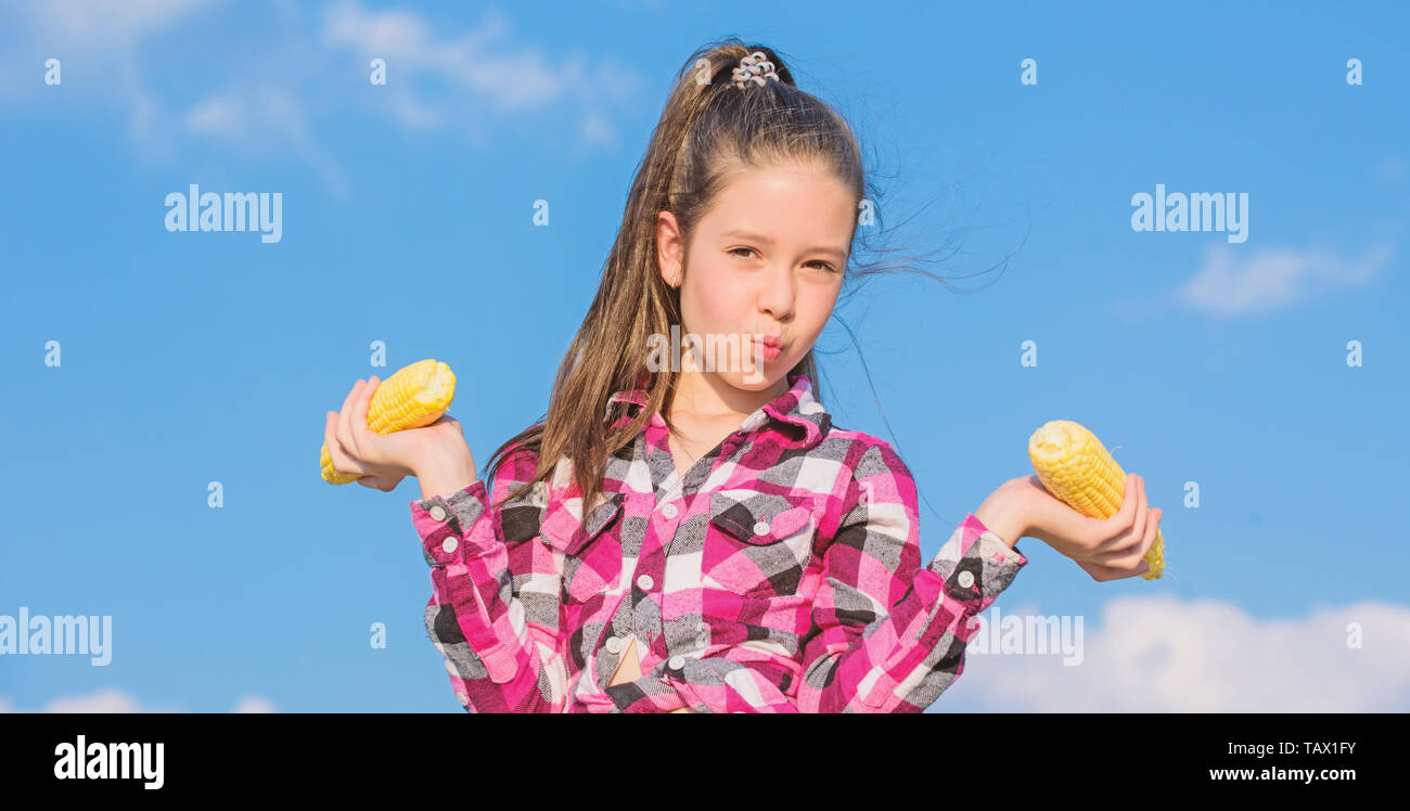 Kid girl hold yellow corn cob on sky background. Girl cheerful hold ...