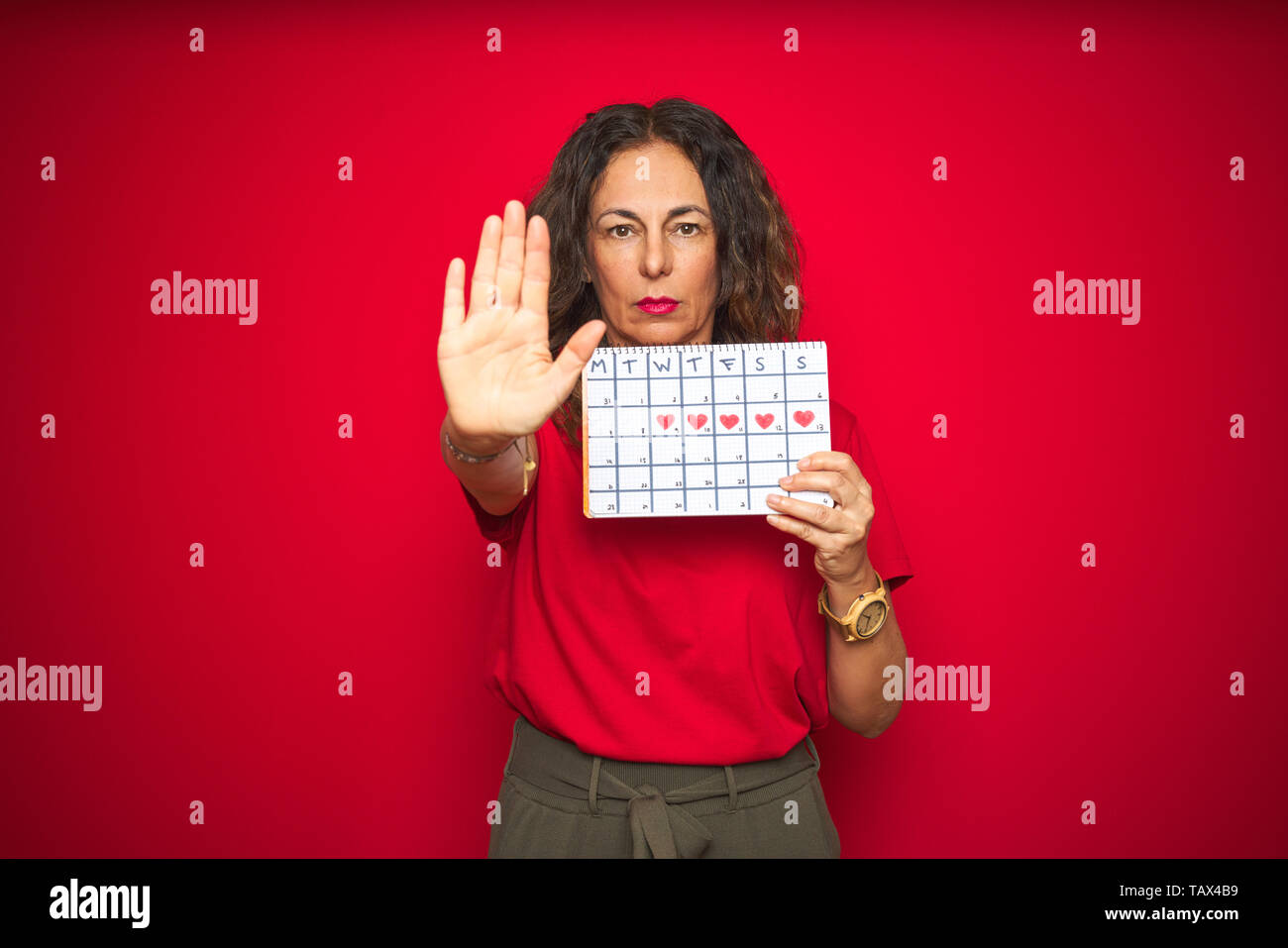 Middle age senior woman holding menstruation calendar over red isolated ...