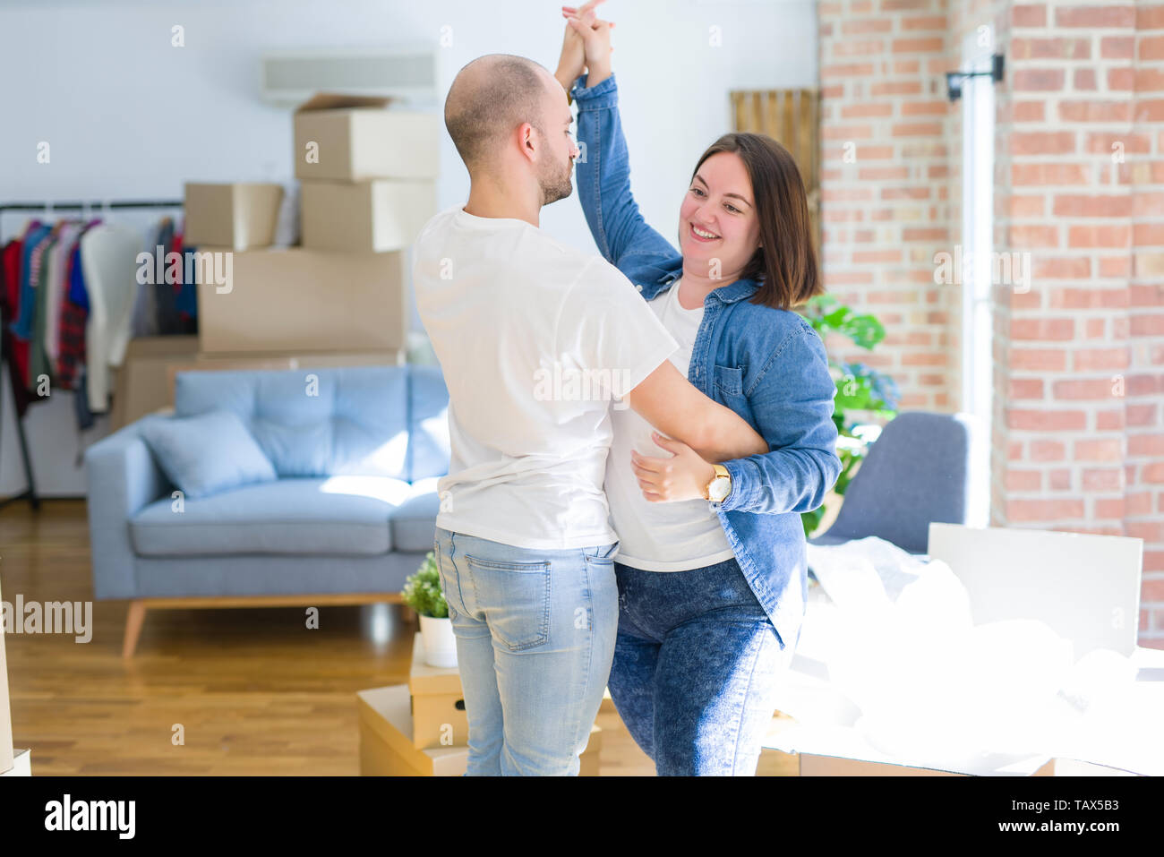 Young couple dancing around cardboard boxes at new home, celebrating ...