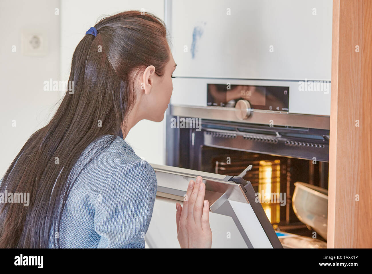 Beautiful woman in the kitchen, waiting with the front of the oven ...