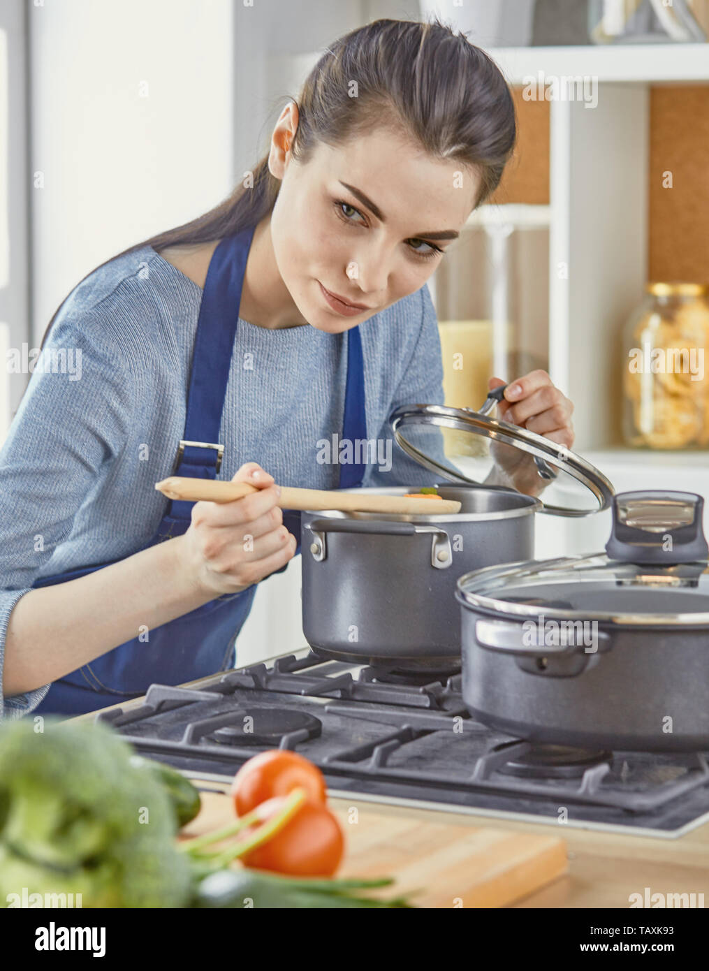 Beautiful girl is tasting food and smiling while cooking in kitchen at ...