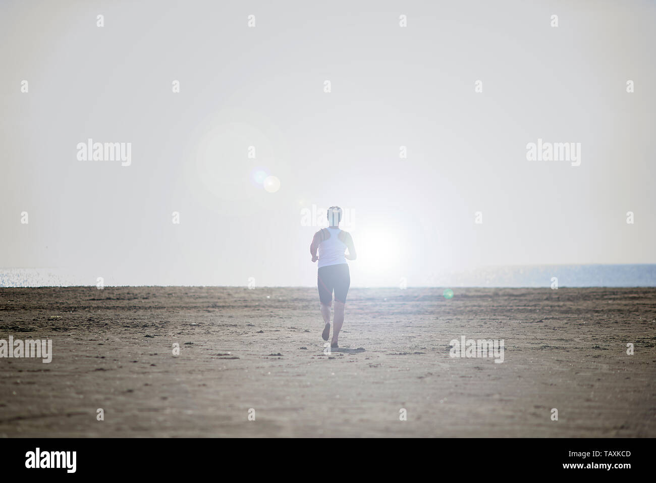 Beautiful shot of a female runner jogging on the beach wearing a black ...