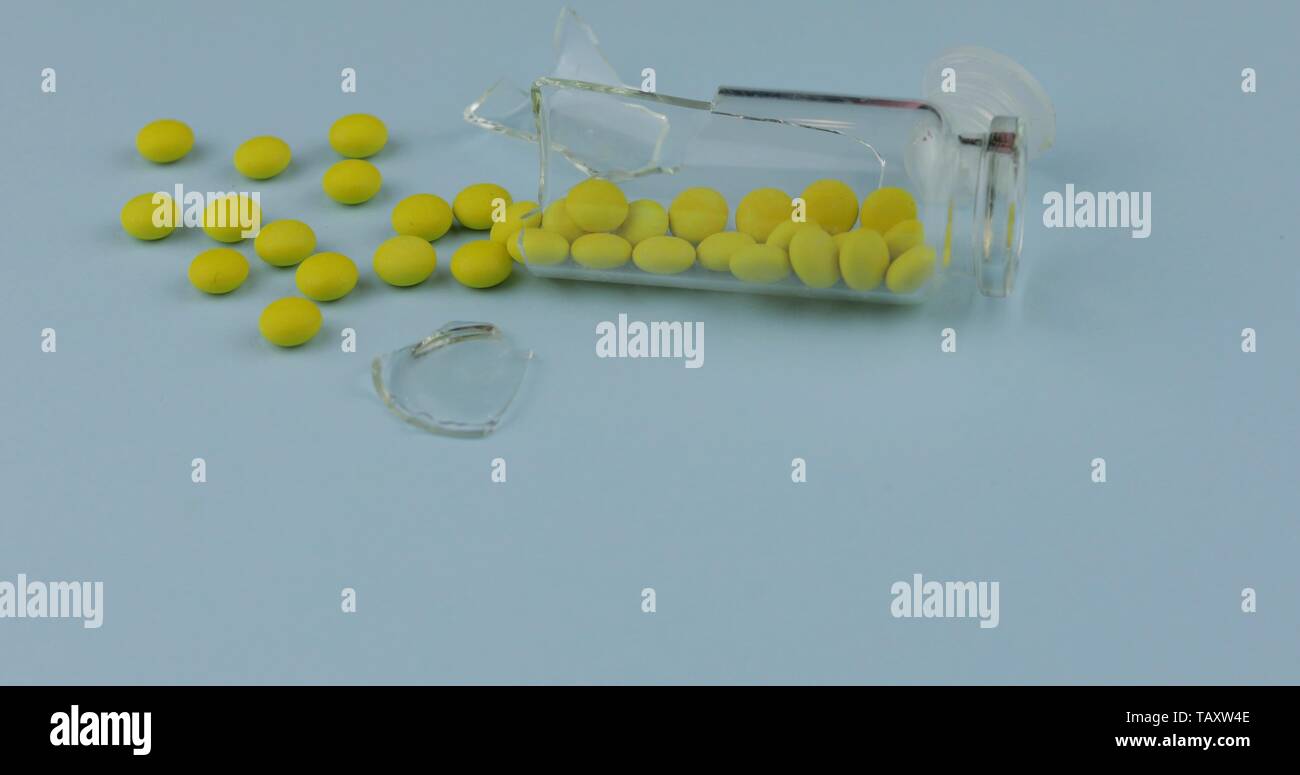 Broken glass jar with many yellow pills and drugs on blue background ...