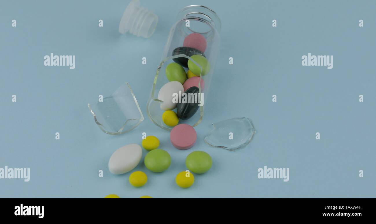 Broken glass jar with many different pills and drugs on blue background ...